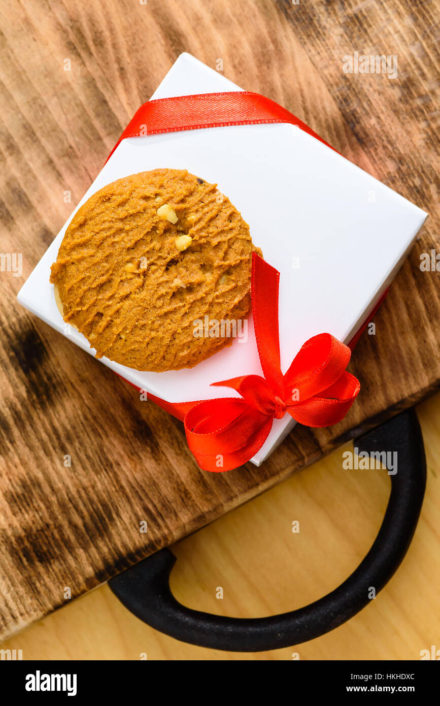 Small white present with red bow and cookie on top of wooden tray or ...