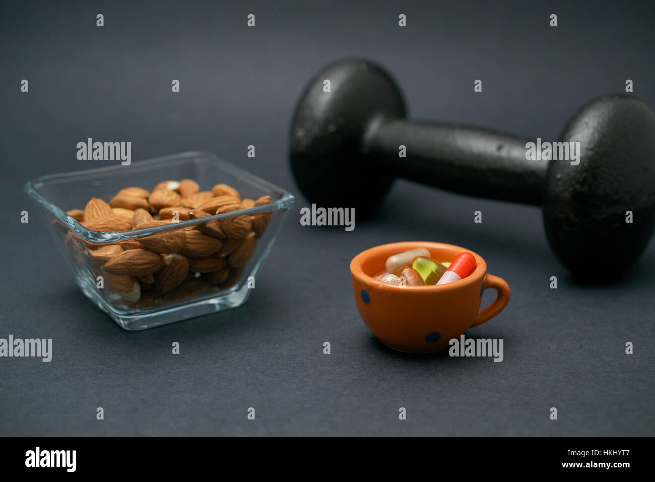 Dumbbell, almonds and dietary supplements on dark background: fitness ...