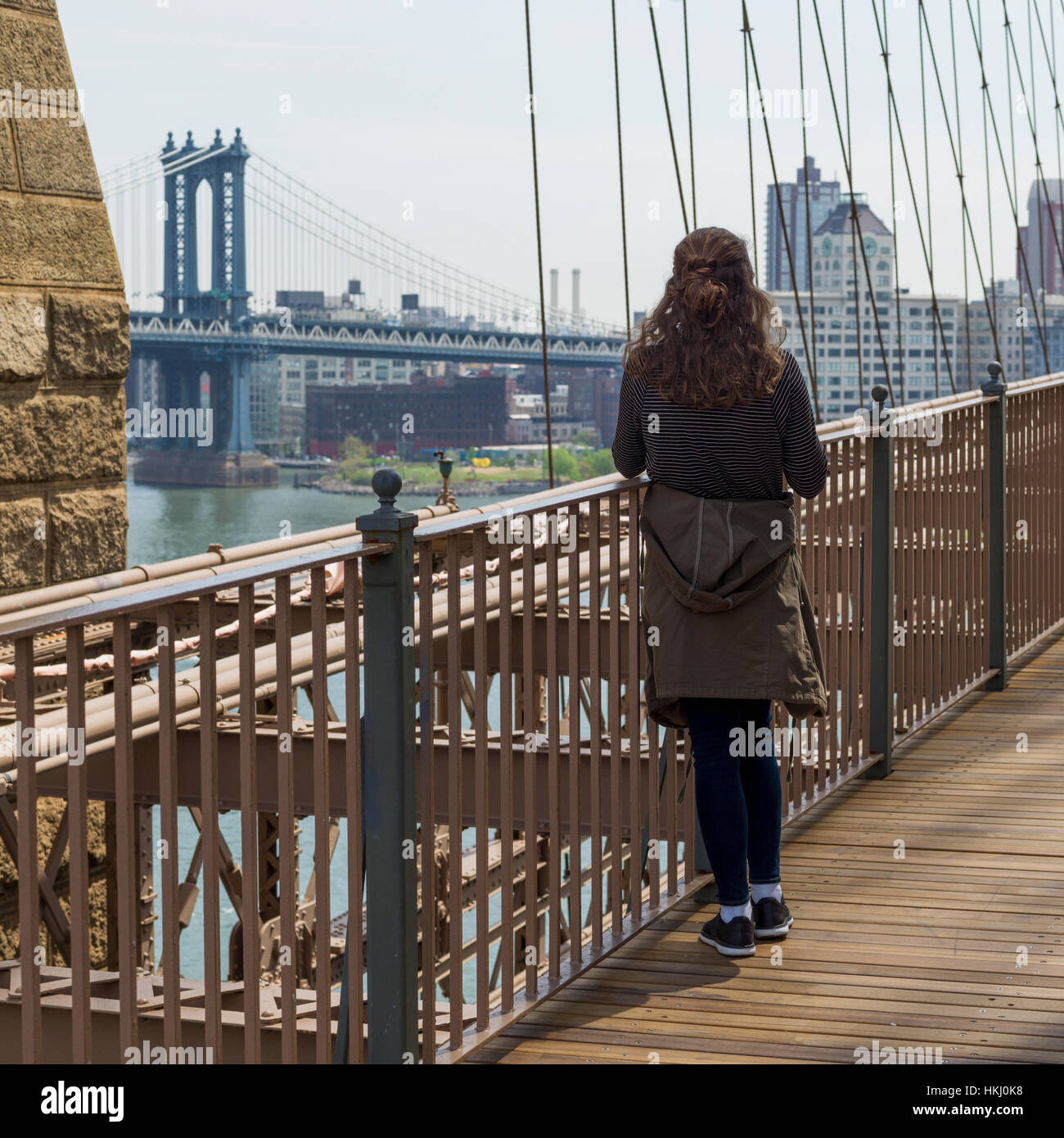 A young woman stands on the Brooklyn Bridge looking out over the East ...