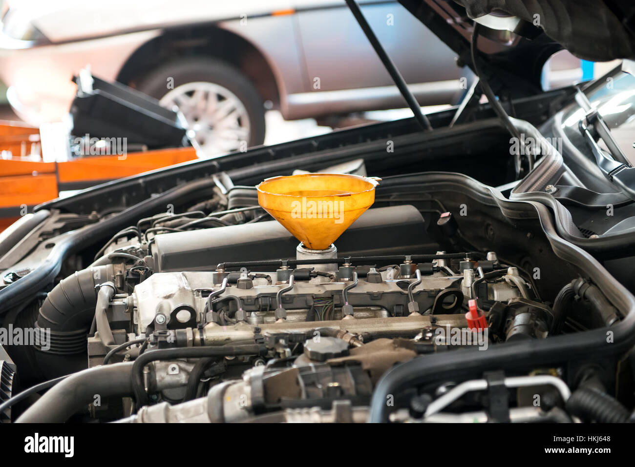 Close-up side view of car engine under opened hood with funnel inserted ...
