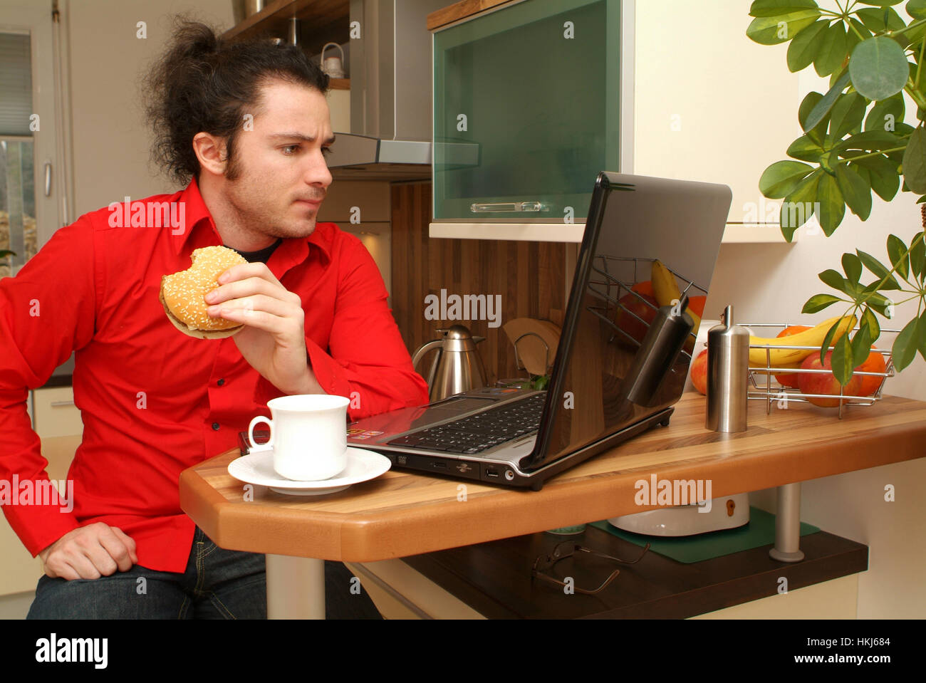 Man eating burger while using laptop Stock Photo - Alamy