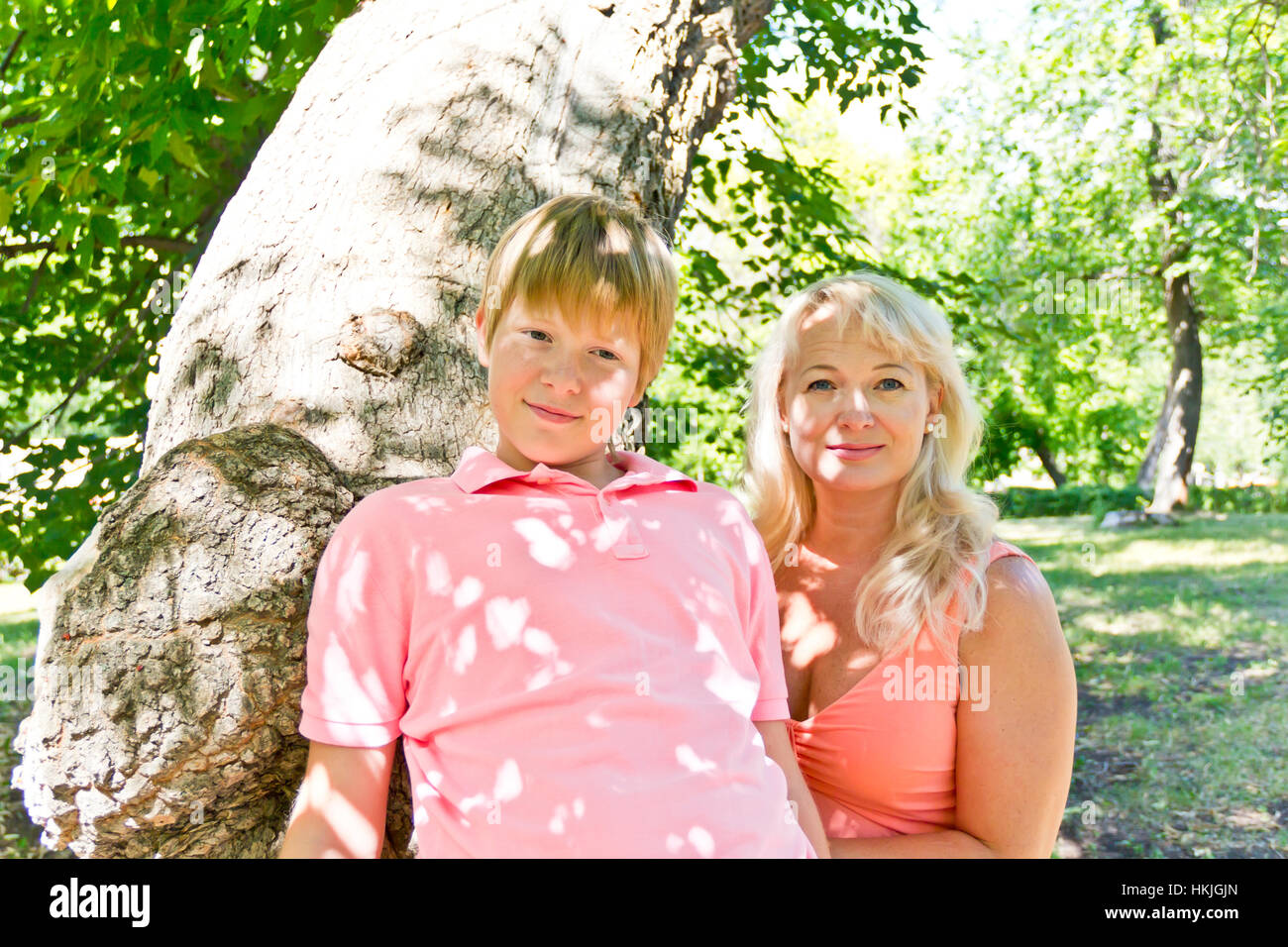 Blond woman and son in pink smiling under green crone of tree Stock ...