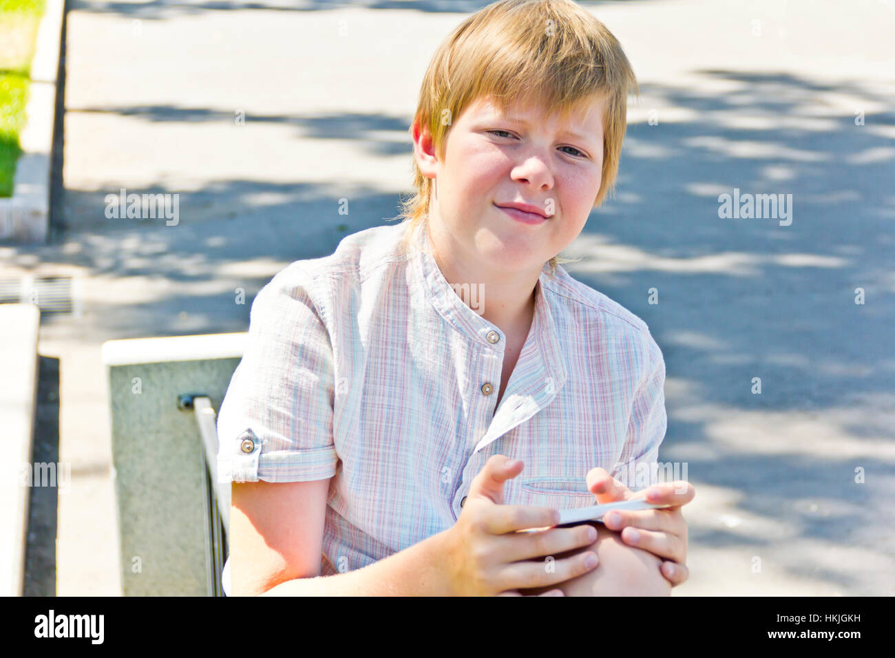 Blond boy with mobile phone sitting on a bench Stock Photo - Alamy