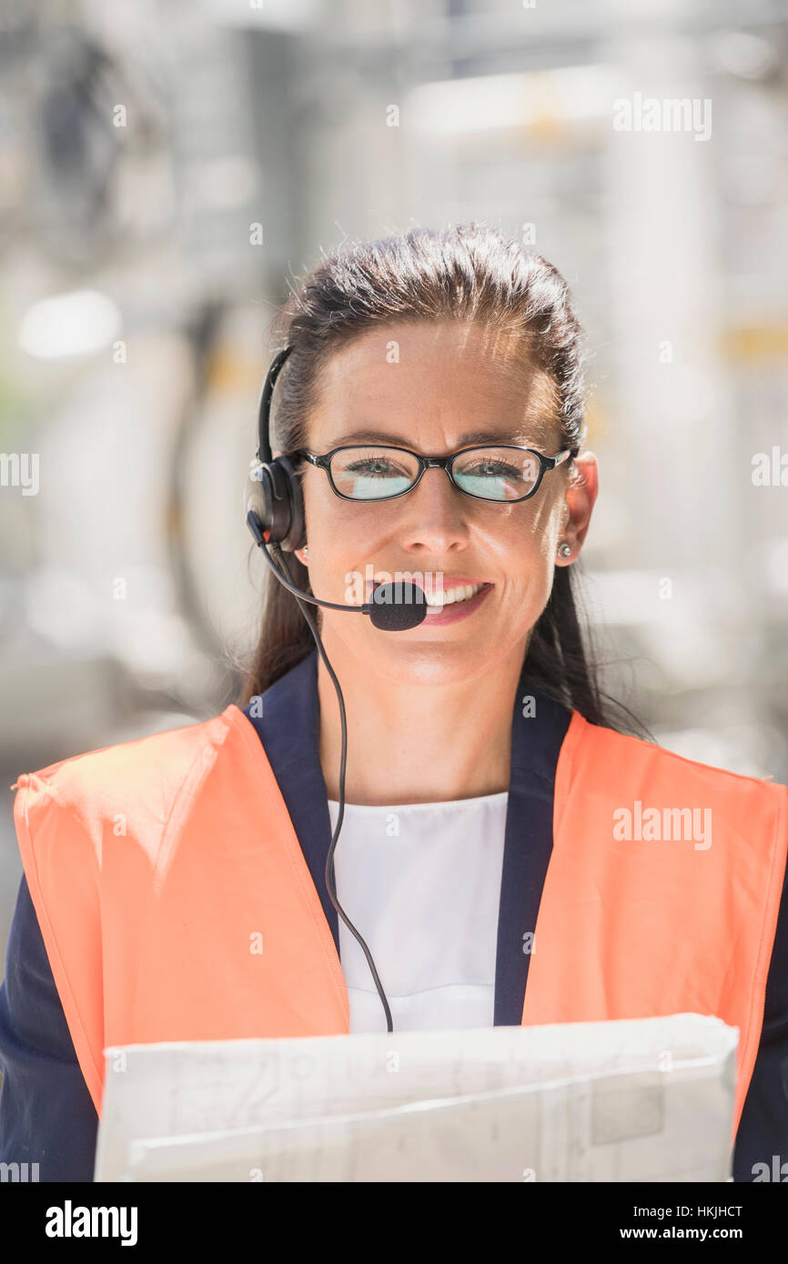 Portrait of a female engineer wearing headset with blueprint at ...