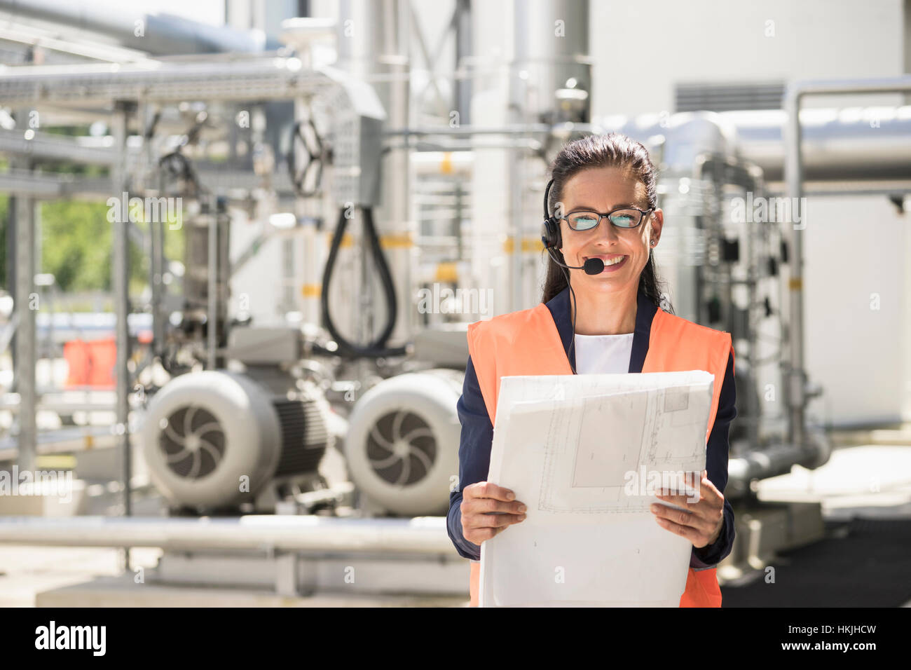 Portrait of a female engineer wearing headset with blueprint at ...