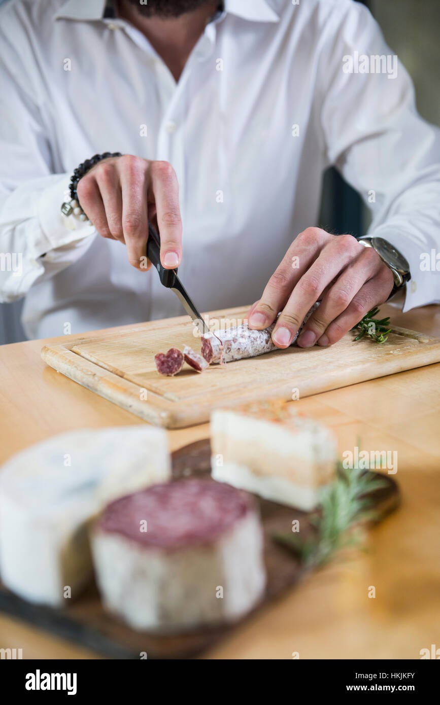 Mid section of a man cutting salami in the kitchen, Bavaria, Germany ...
