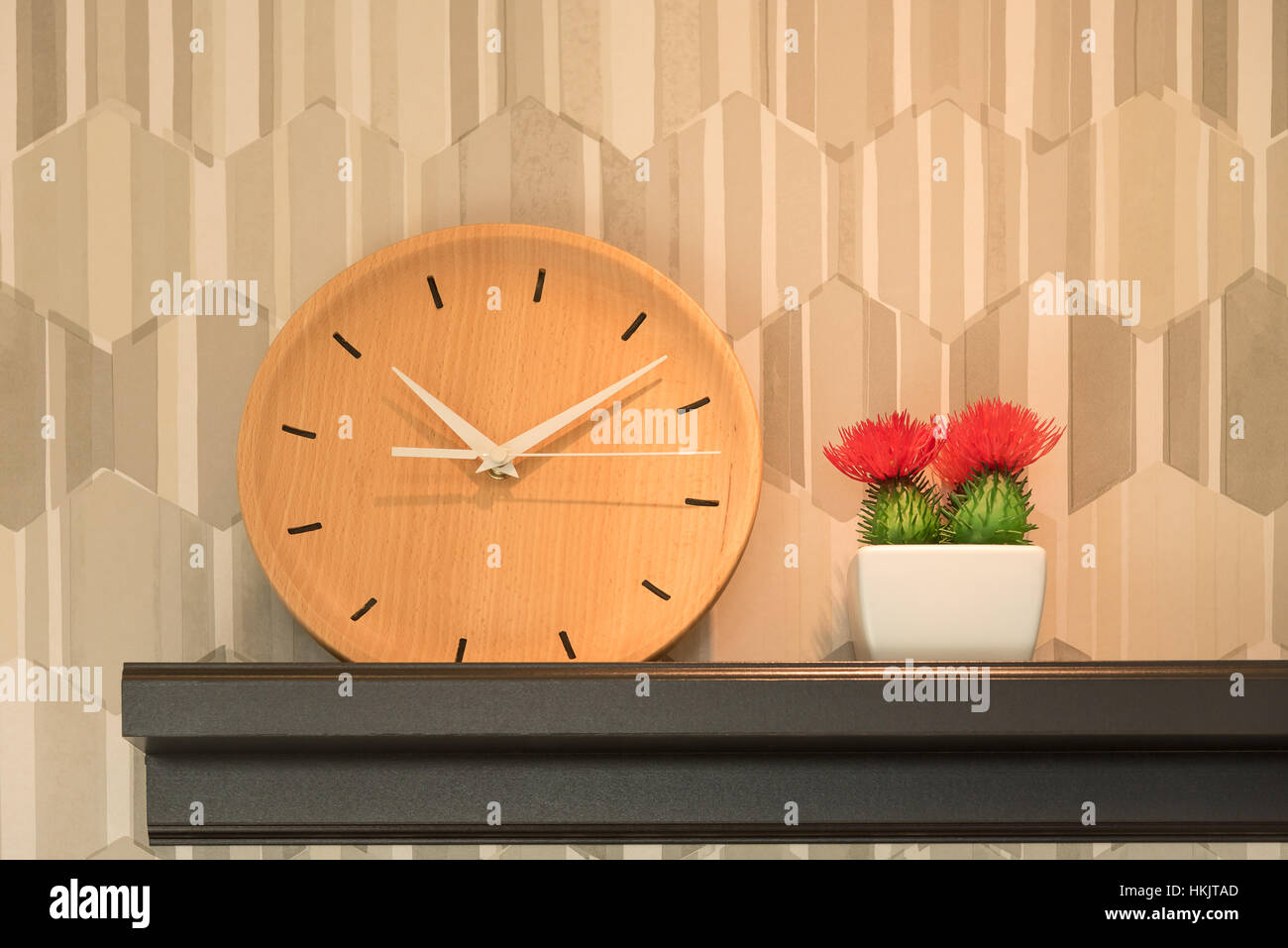 A wooden clock put on black metal shelf standing out from wallpaper ...
