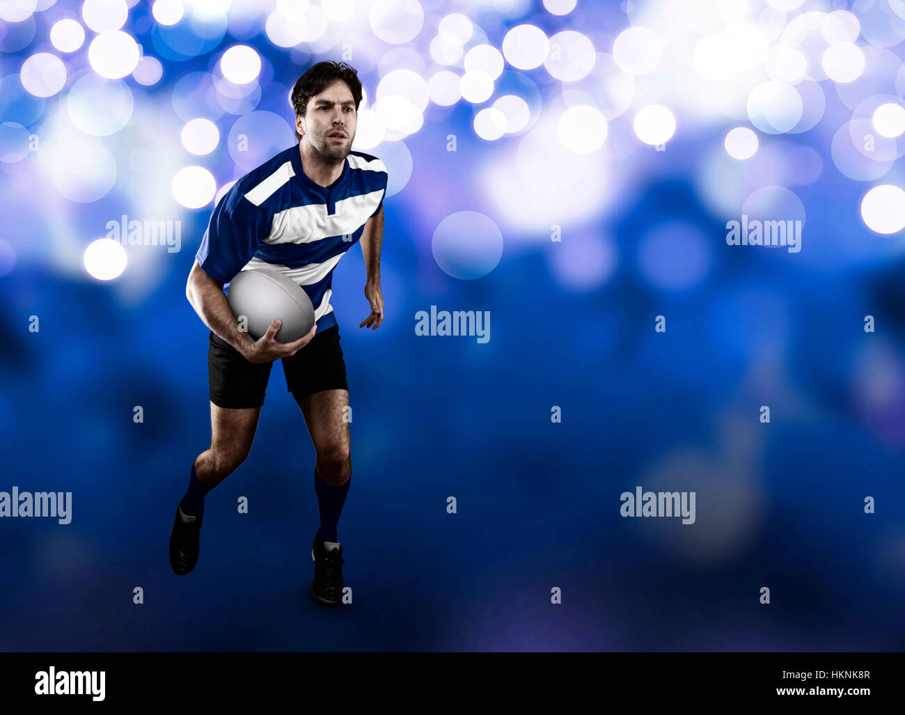 Rugby player in a blue uniform running on a blue lights background ...