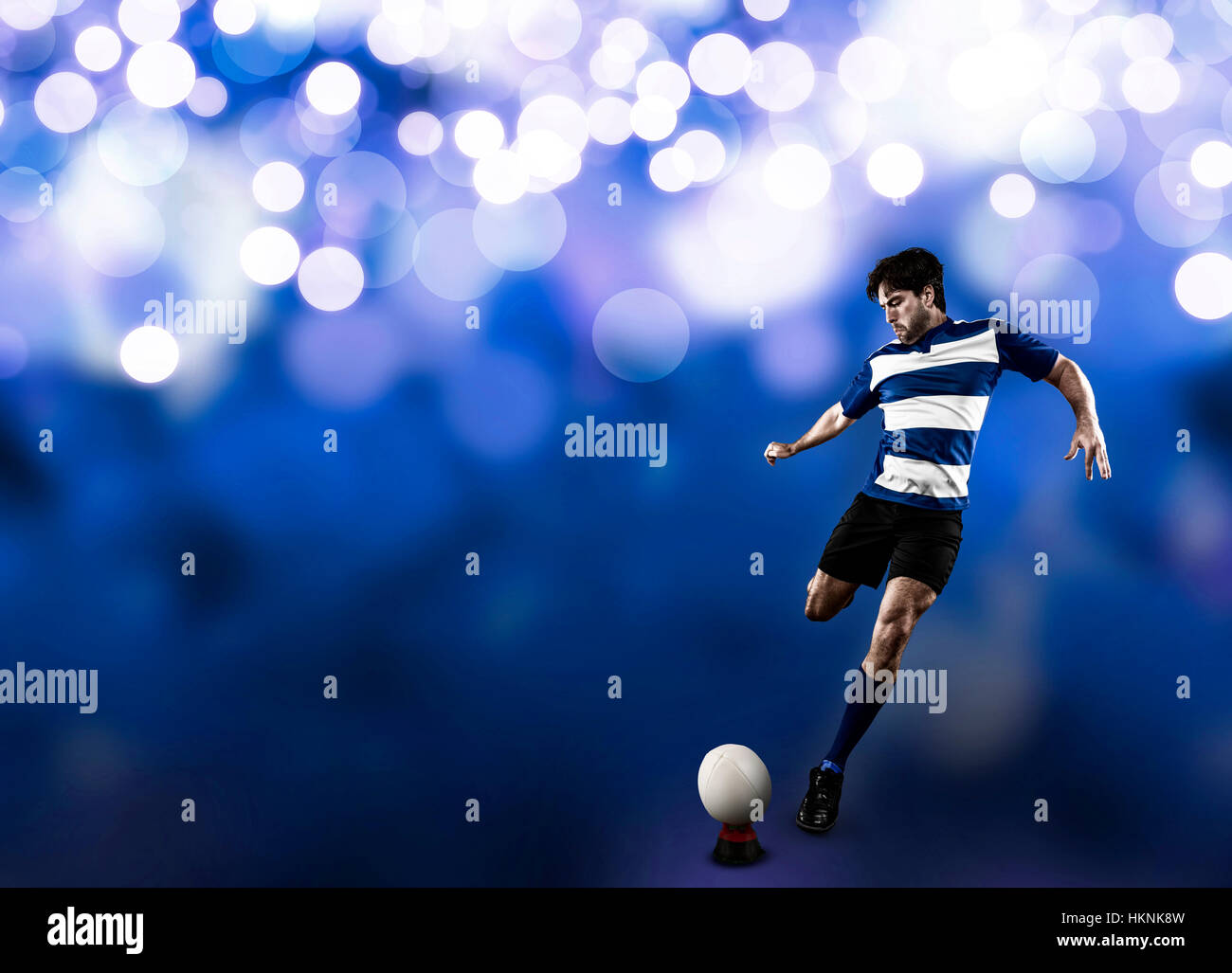 Rugby player in a blue uniform kicking a ball on a blue lights ...