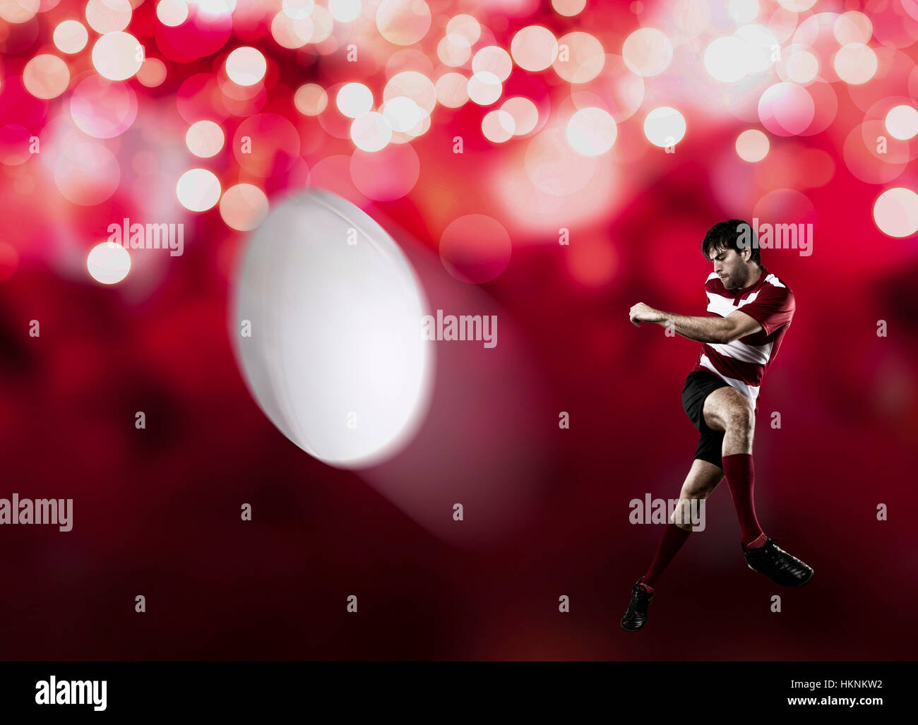 Rugby player in a red uniform kicking a ball on a red lights background ...