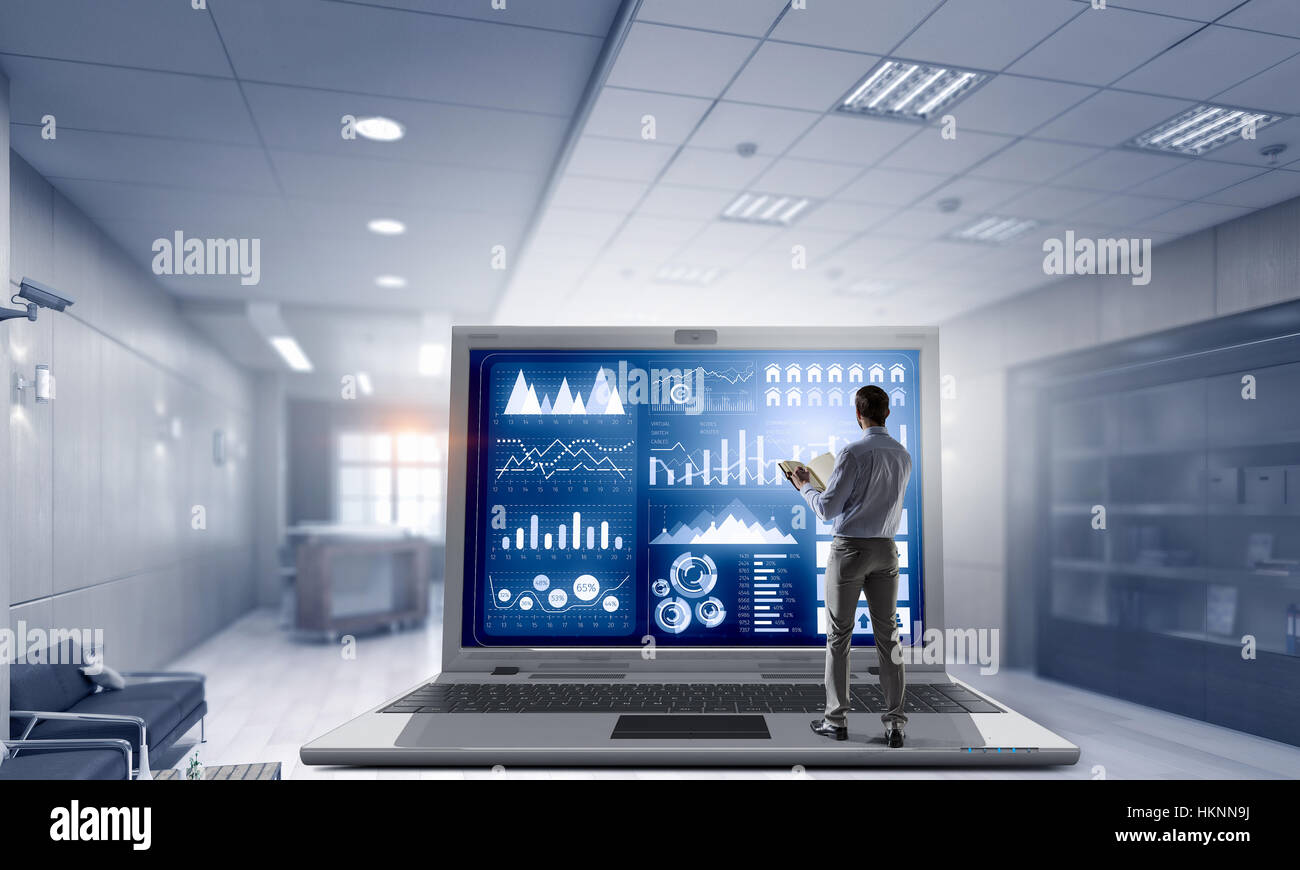 Young businessman and huge laptop with infographs on screen. Mixed ...