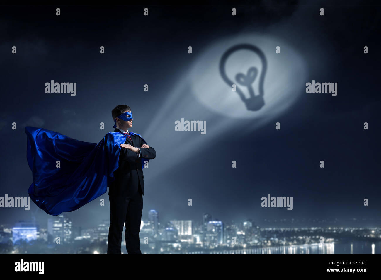 Young businessman in mask and cape and bulb sign glowing in sky Stock ...
