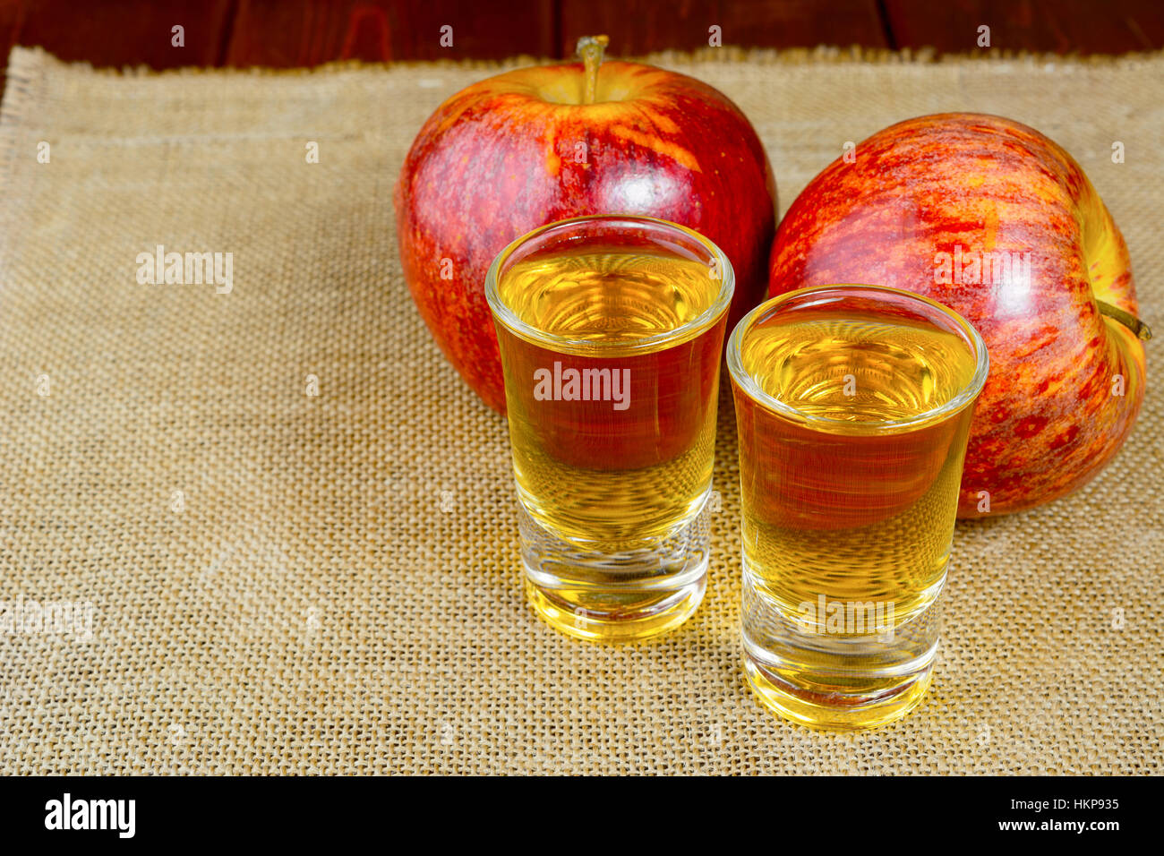 Two schnapps drinks and red apples on the rustic burlap background ...