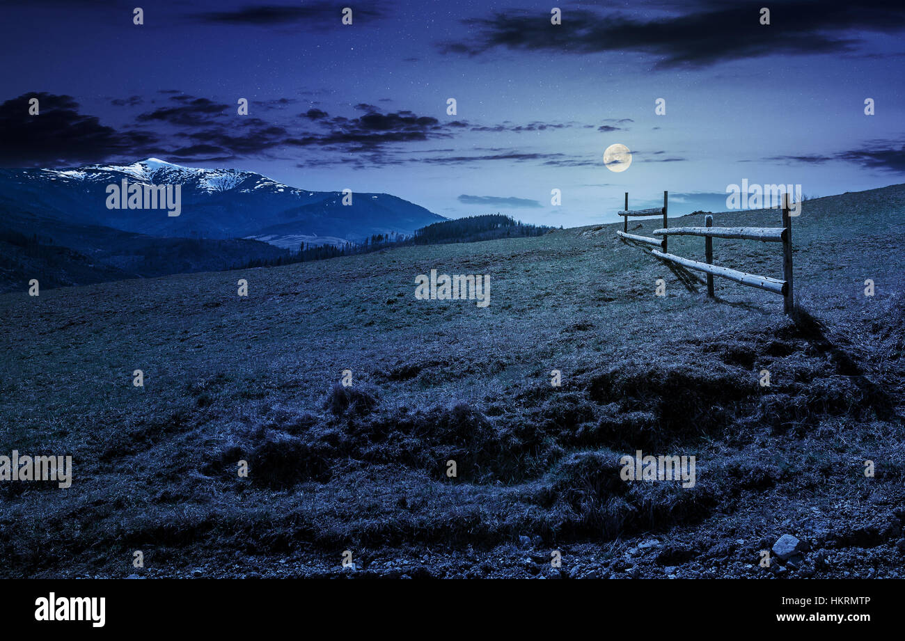 wooden fence on grassy hillside near mountains with snowy peaks in ...