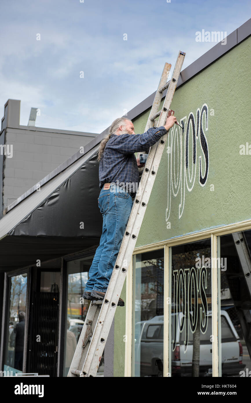 Sign painter on a ladder painting a store name on a Main Street ...