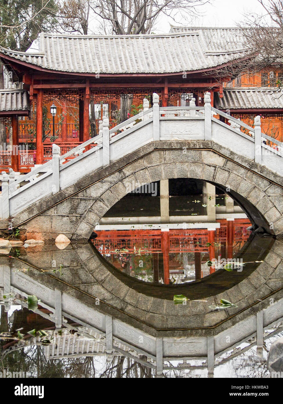A traditional Chinese bridge reflects in a calm pond in a memorial park ...