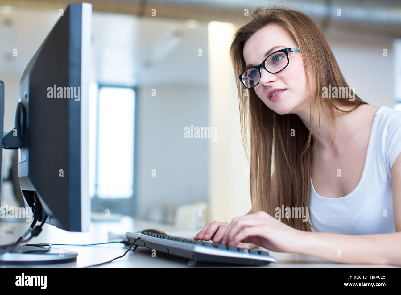 Pretty, female student looking at a desktop computer screen, learning ...