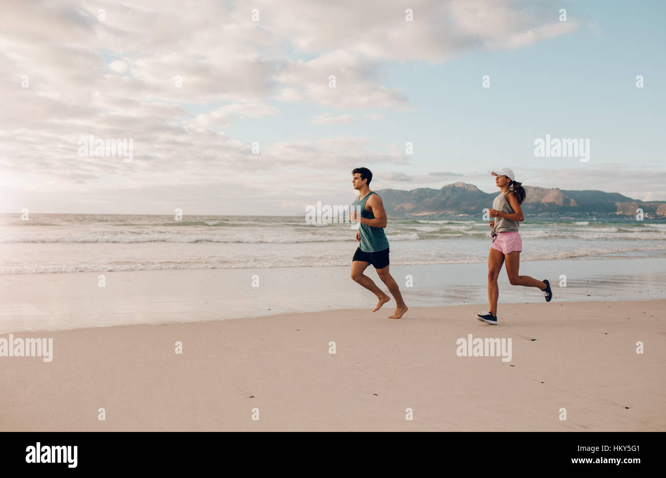Full length shot of fit young man and woman running on the beach ...