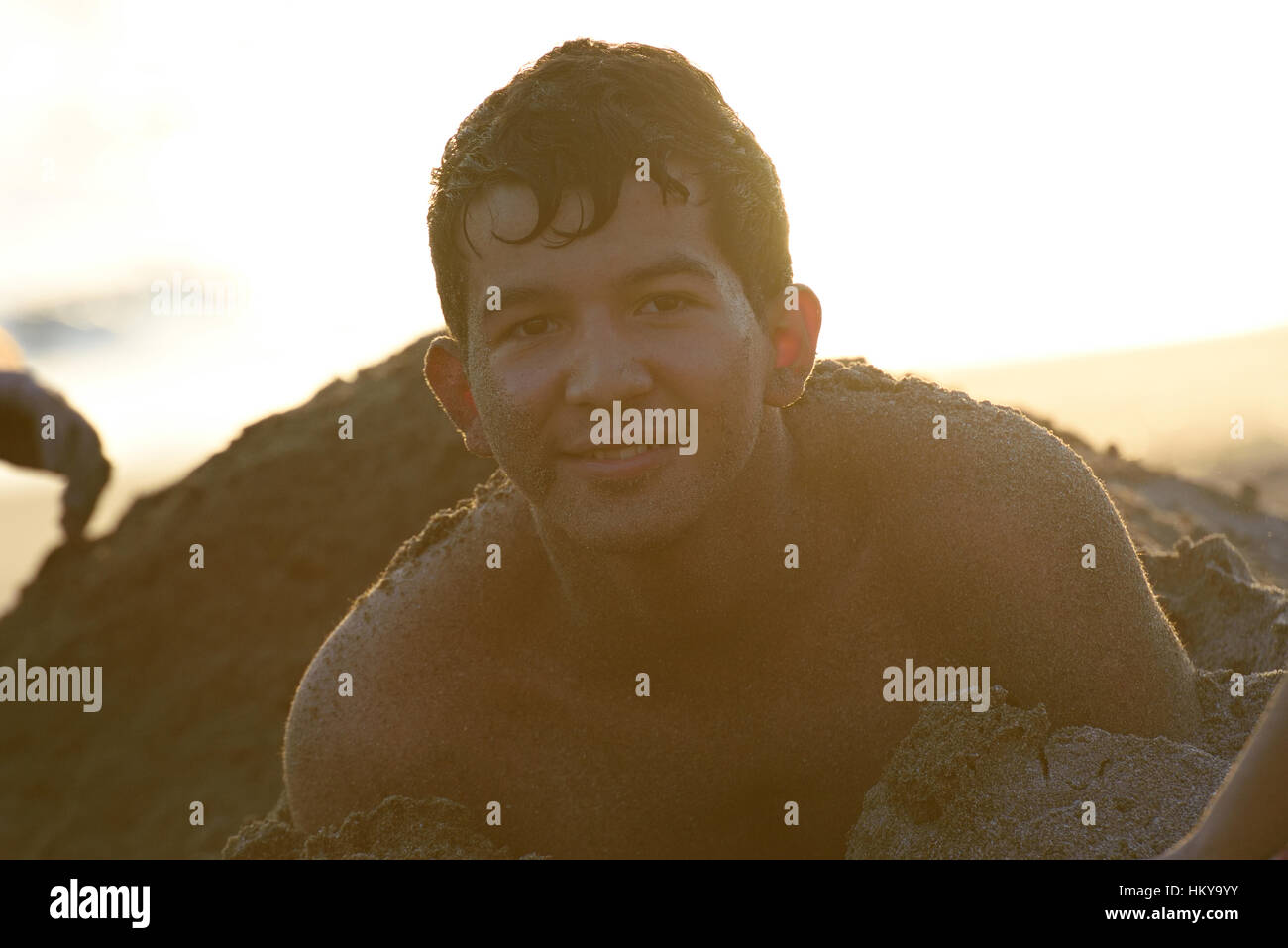 happy guy teenager buried in sand light of sun Stock Photo - Alamy