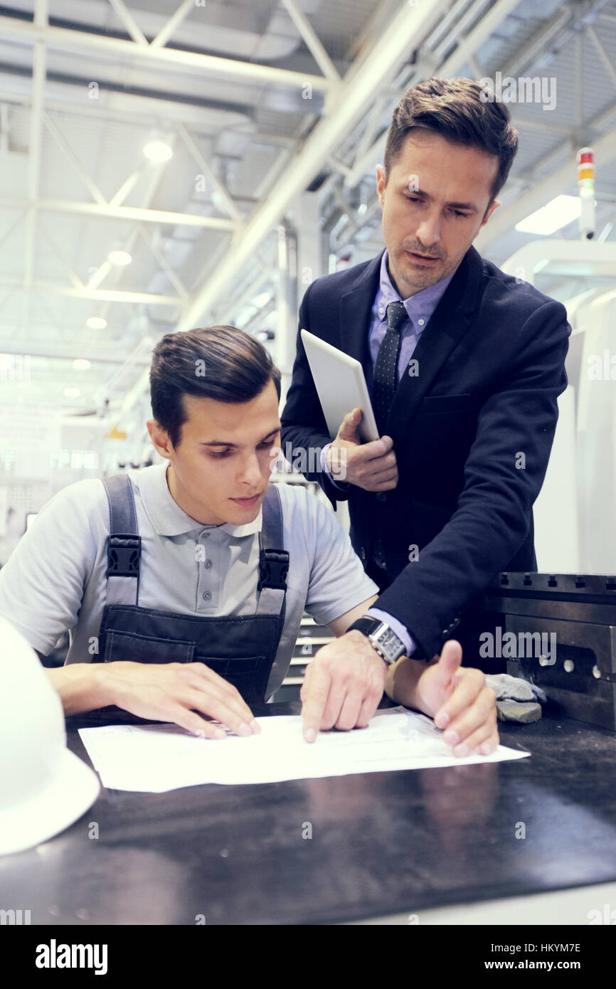 Manager and worker looking at technical documents at factory Stock ...