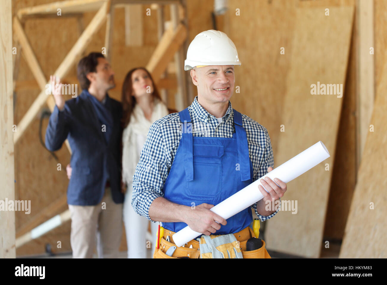 Worker with house design plans and young couple at construction site ...