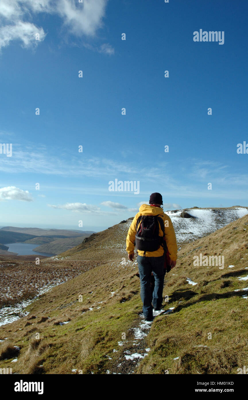 Rear view of hill walker traversing narrow mountain path on a bright ...