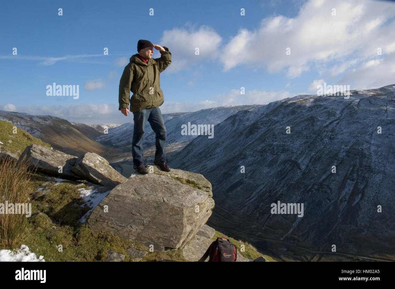 Hill walker standing on rocky outcrop looking across valley to snow ...