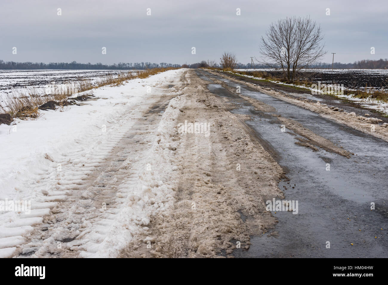 Winter landscape with remote empty road covered with melting snow in ...