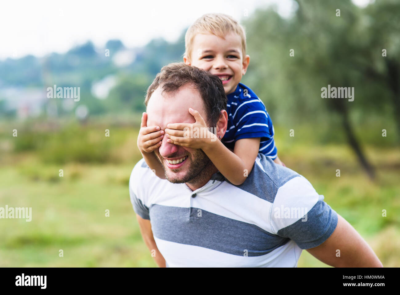 Boy closes hands eyes father. Happy little boy enjoying with riding on ...