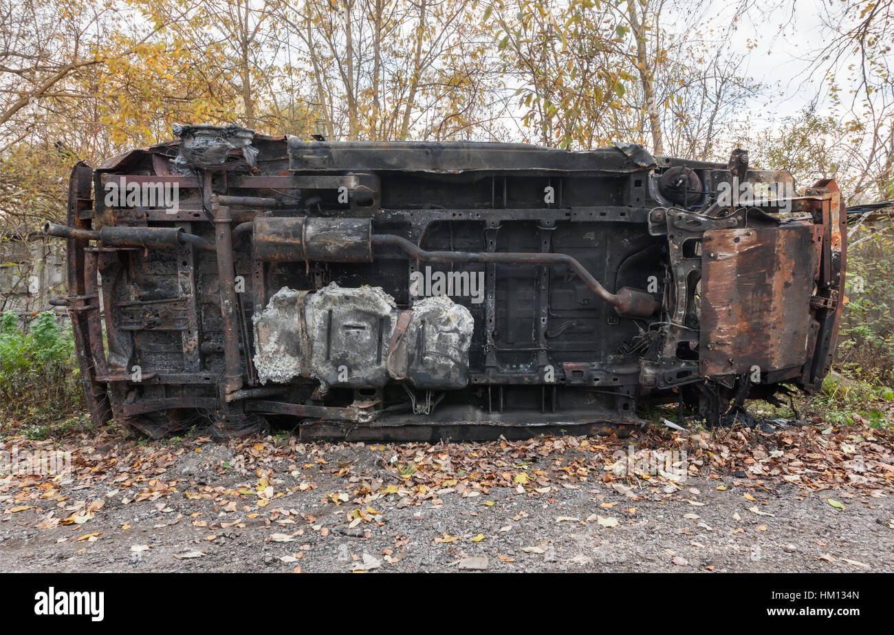 Rusty burned out SUV on it side. On the background of trees and fallen ...