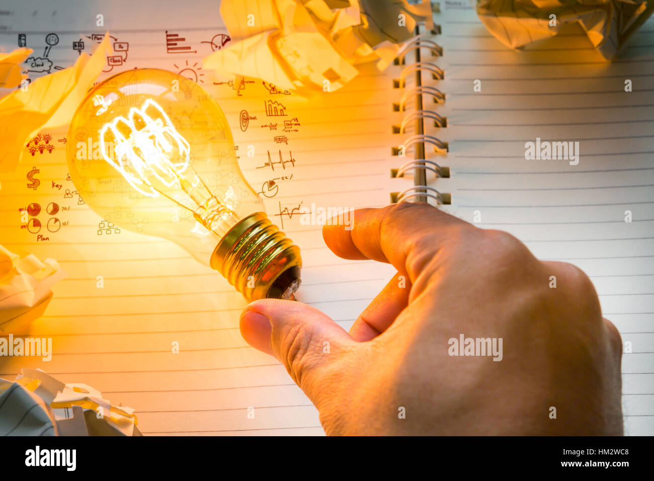Hand pick light bulb with drawing graph over Note book on wood table ...