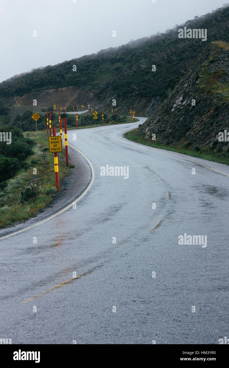A danger warning sign on the side of a wet road in the Alpine region of ...