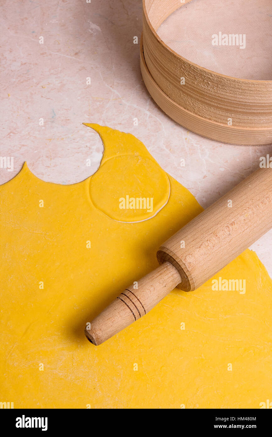 Fresh prepared yellow rolled out dough with white flour and wooden ...
