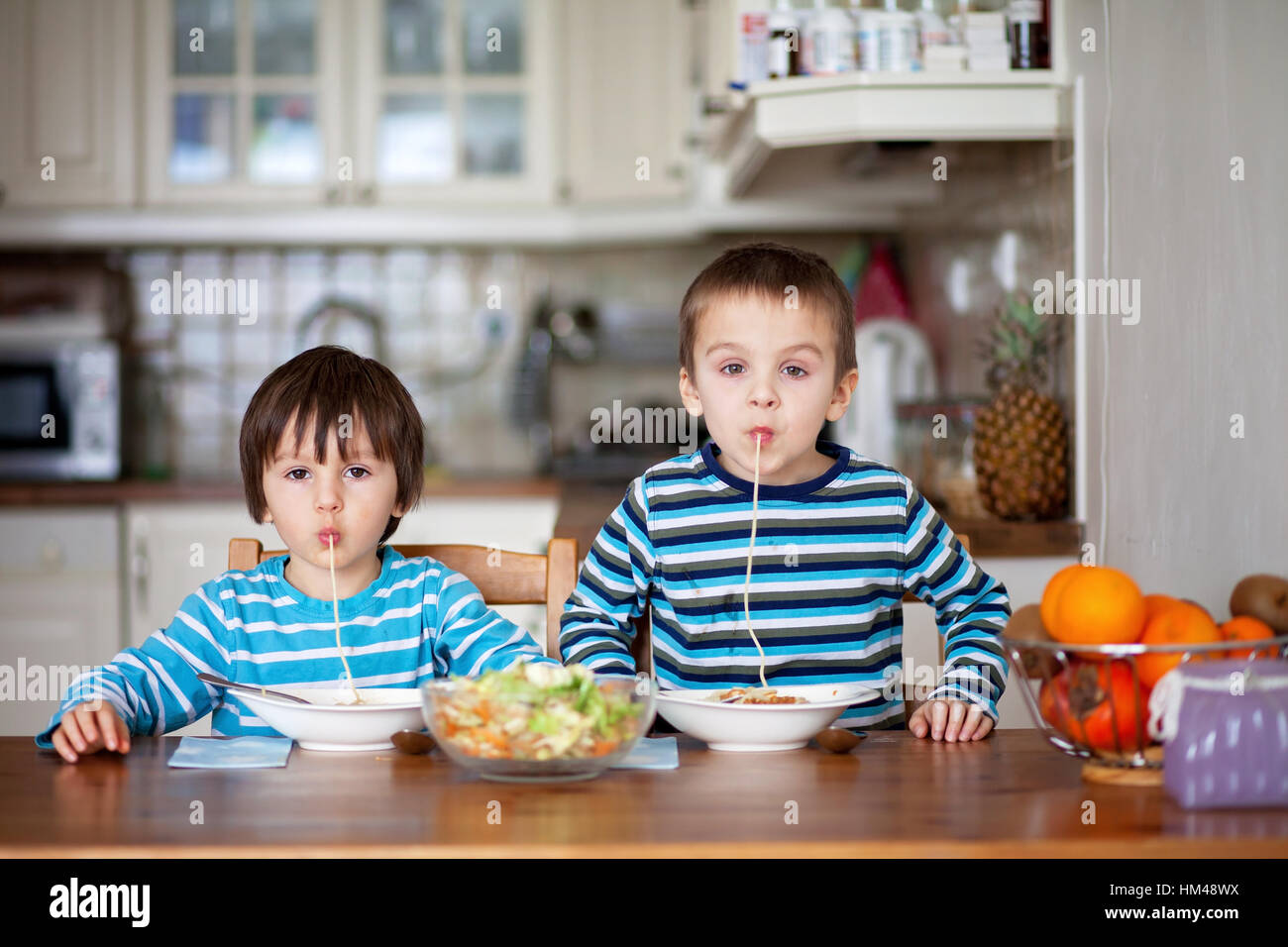 Two sweet children, boy brothers, having for lunch spaghetti at home ...