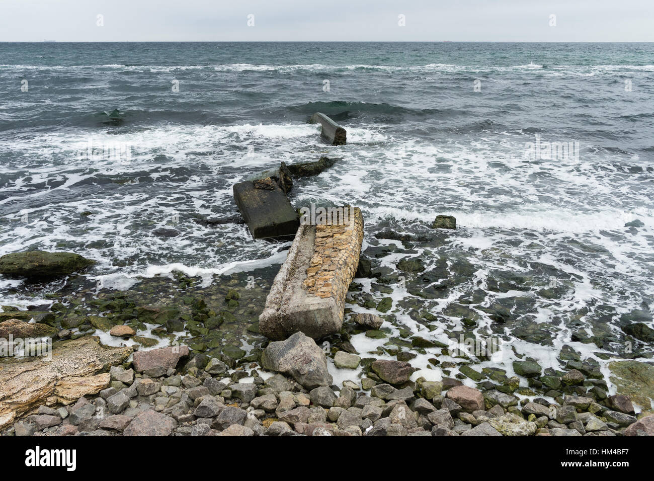 Broken concrete slabs on the rocky shore among the rocks and waves ...