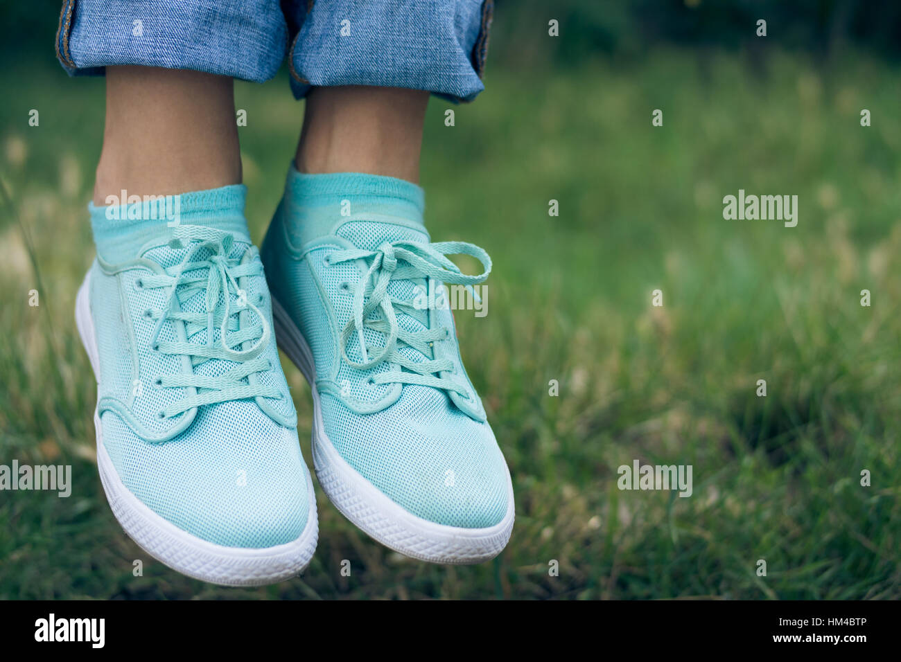 Female legs in jeans and sport shoe floating in the air above the green ...