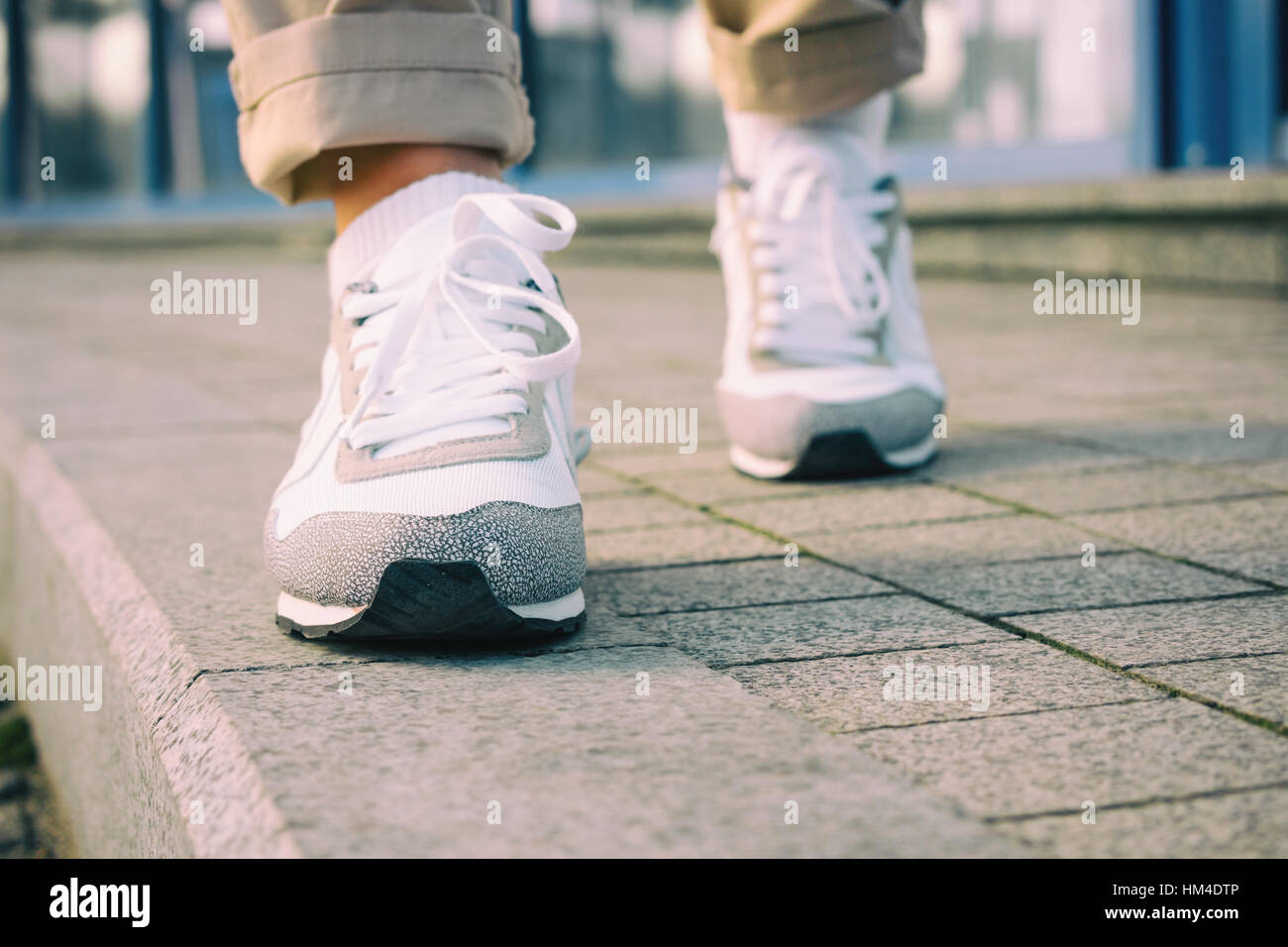 Female feet in white sneakers walking on the sidewalk, low angle, retro ...
