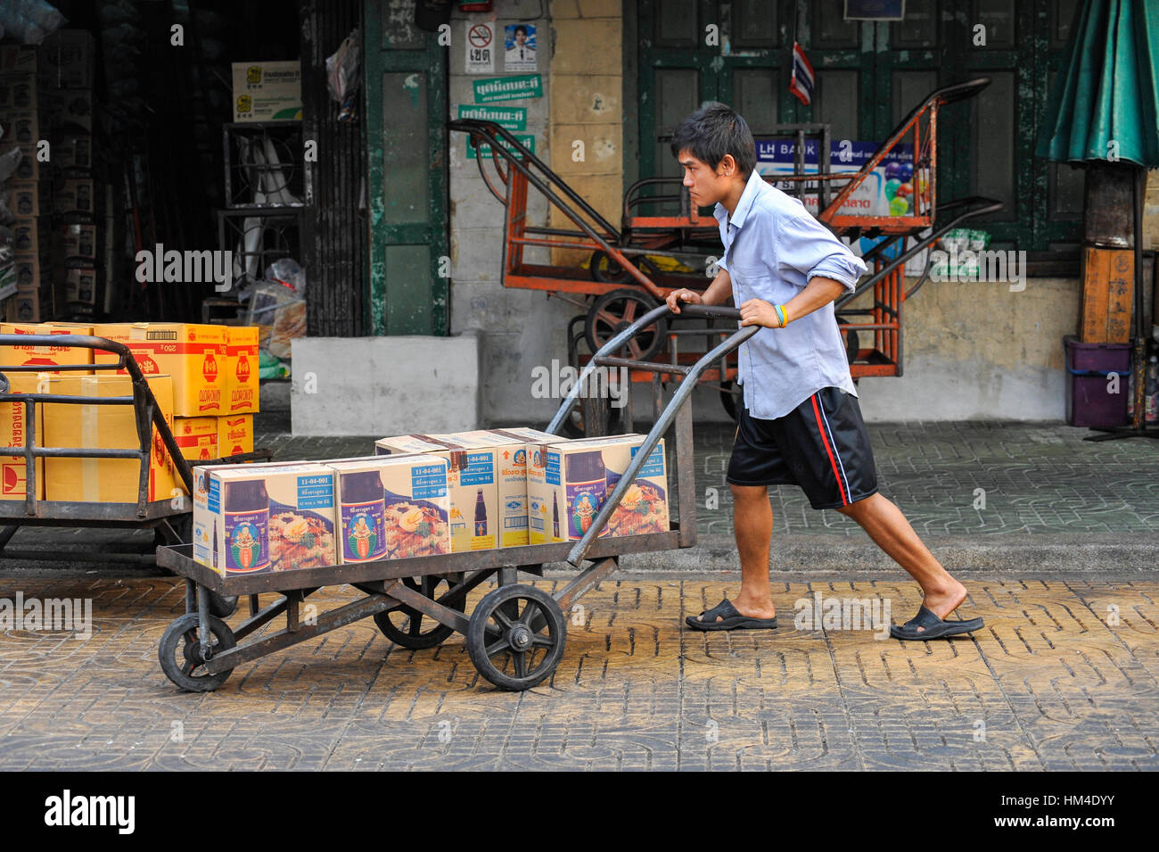 Bangkok market labourer pushing cart loaded with boxes (of soya sauce ...