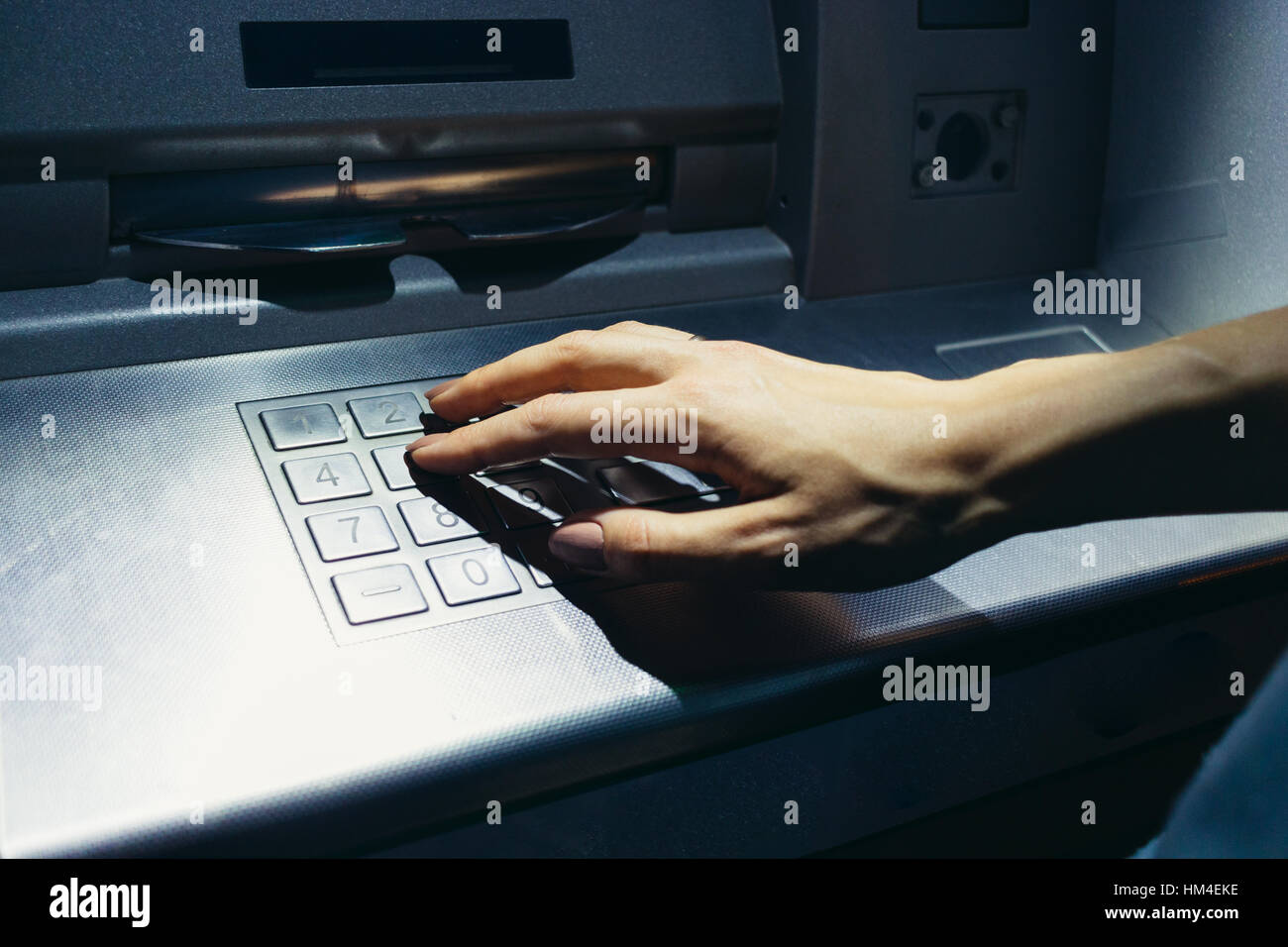 Woman's hand enters the secret code at the ATM on the street at night ...