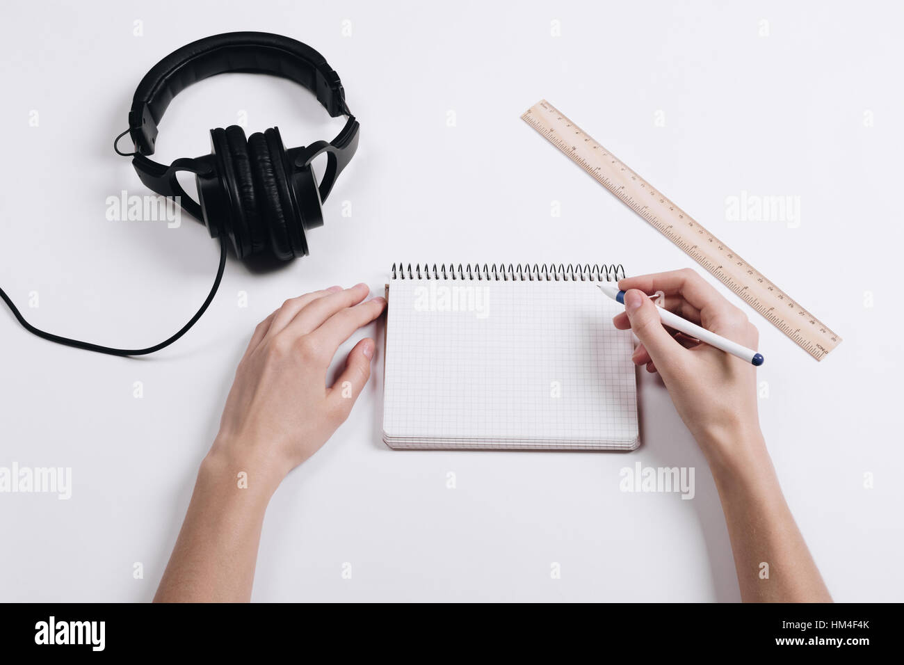 On a white desk are headphones, a ruler and a notebook, female hands ...