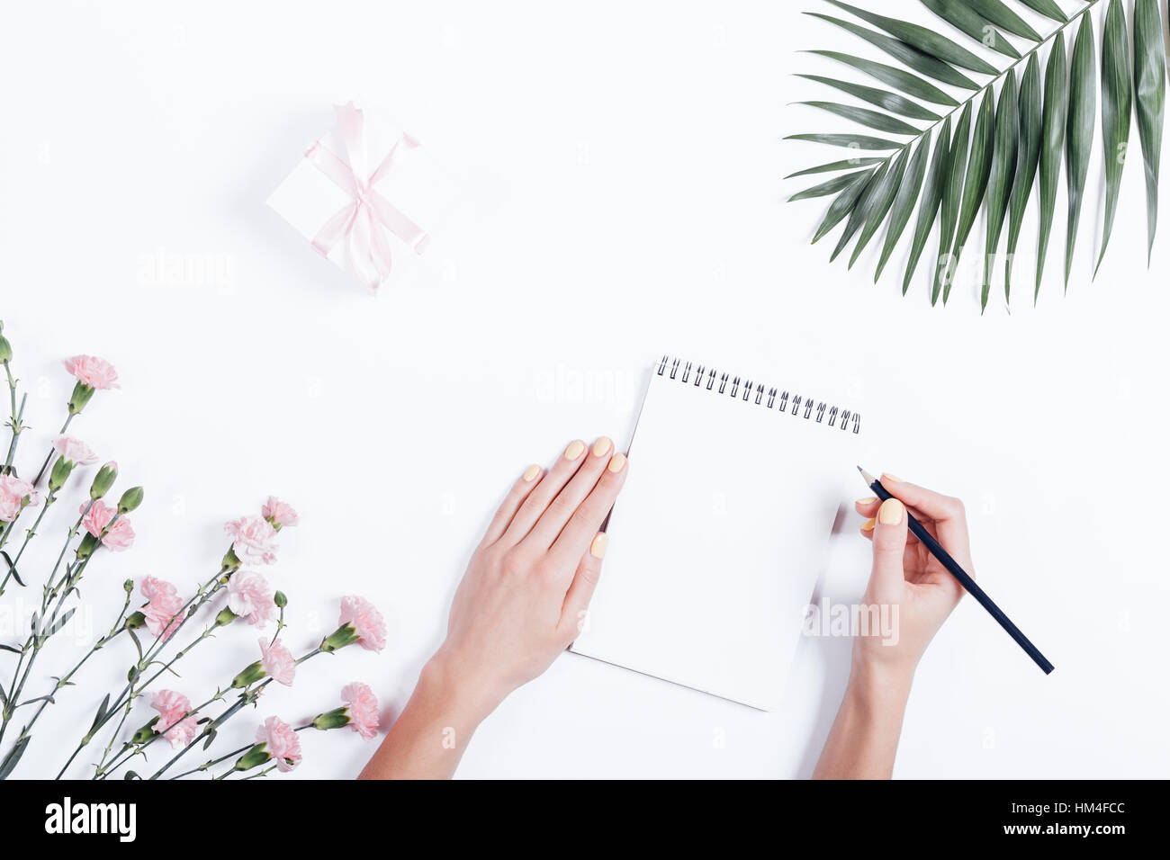 Woman's hand writing in a notebook at the desk, top view. On the white ...