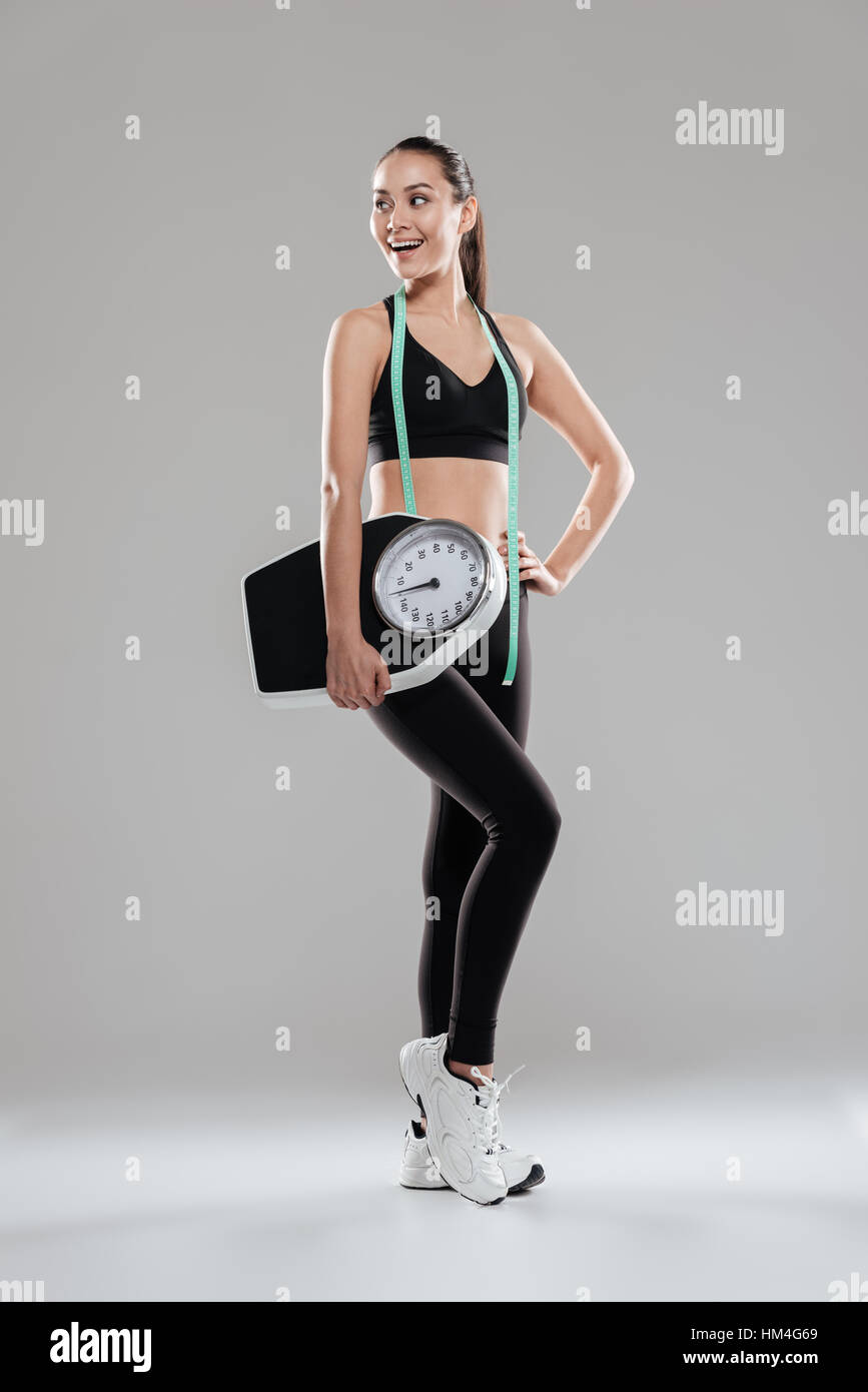 Full length of happy young woman athlete with weighing scale and ...