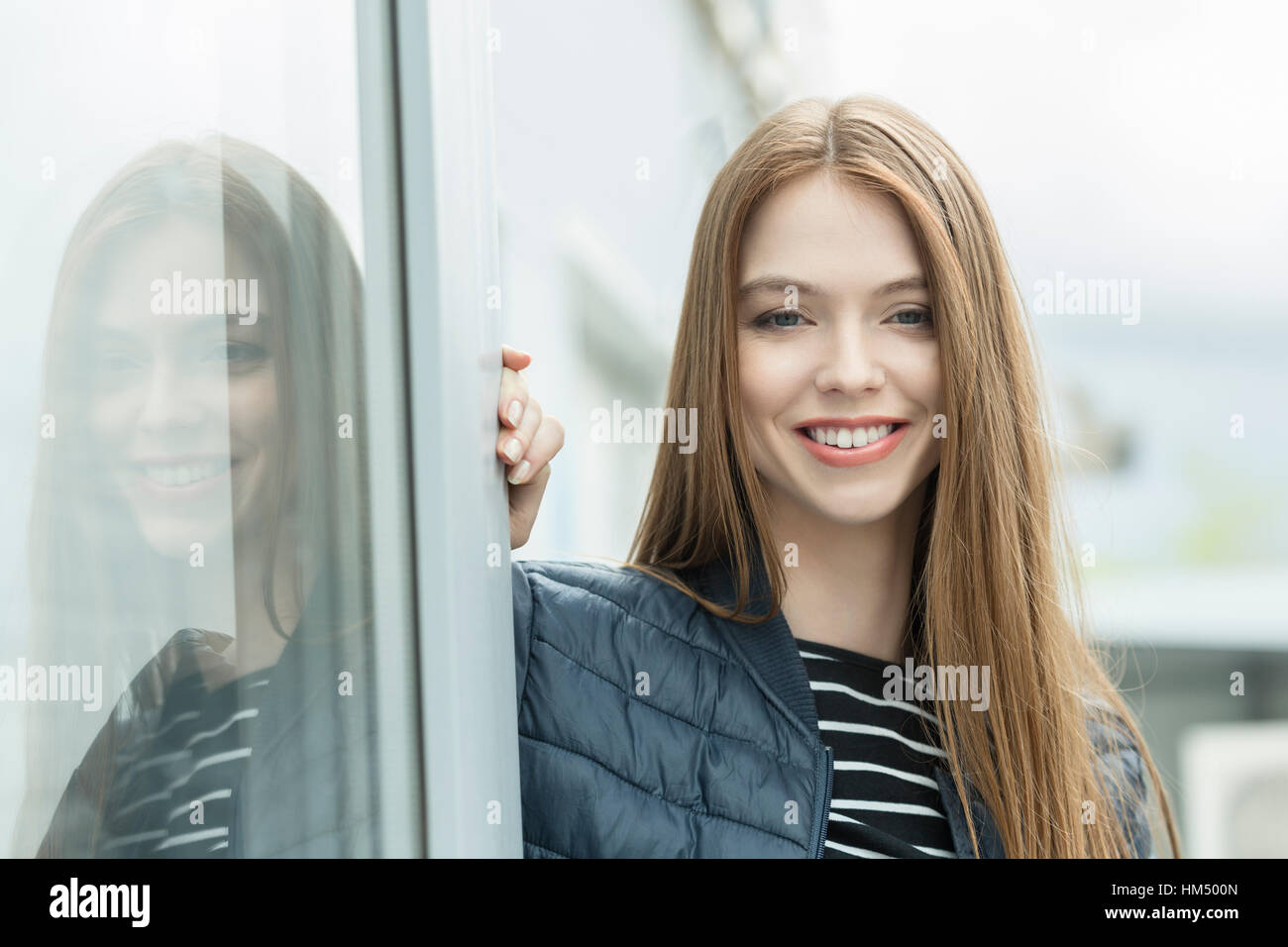 Portrait of young woman standing by window Stock Photo - Alamy