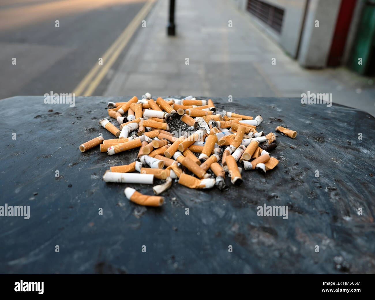 A collection of cigarette butts stubbed out on top of a rubbish bin ...