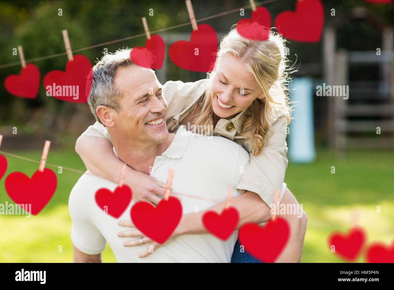 Composite image of red hanging heart and man giving a piggyback to ...