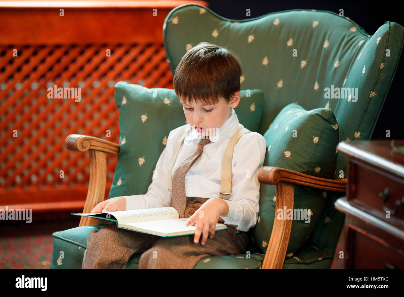 Cute little boy reading book on armchair Stock Photo - Alamy