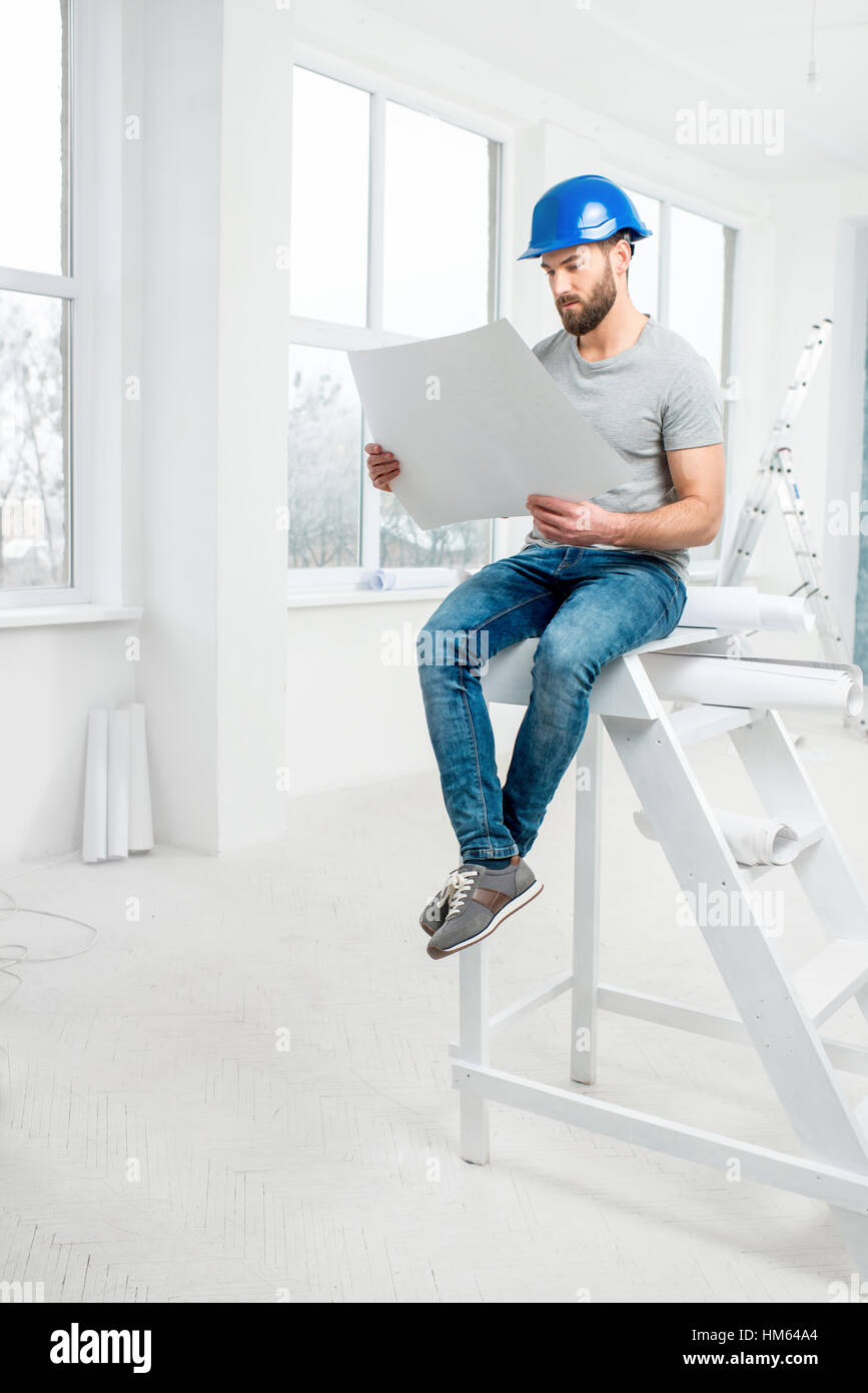 Handsome repairman or builder in helmet working with drawings on ...