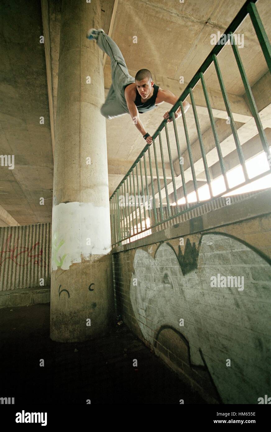 A parkour freerunning athlete vaulting a rail amongst concrete walls ...