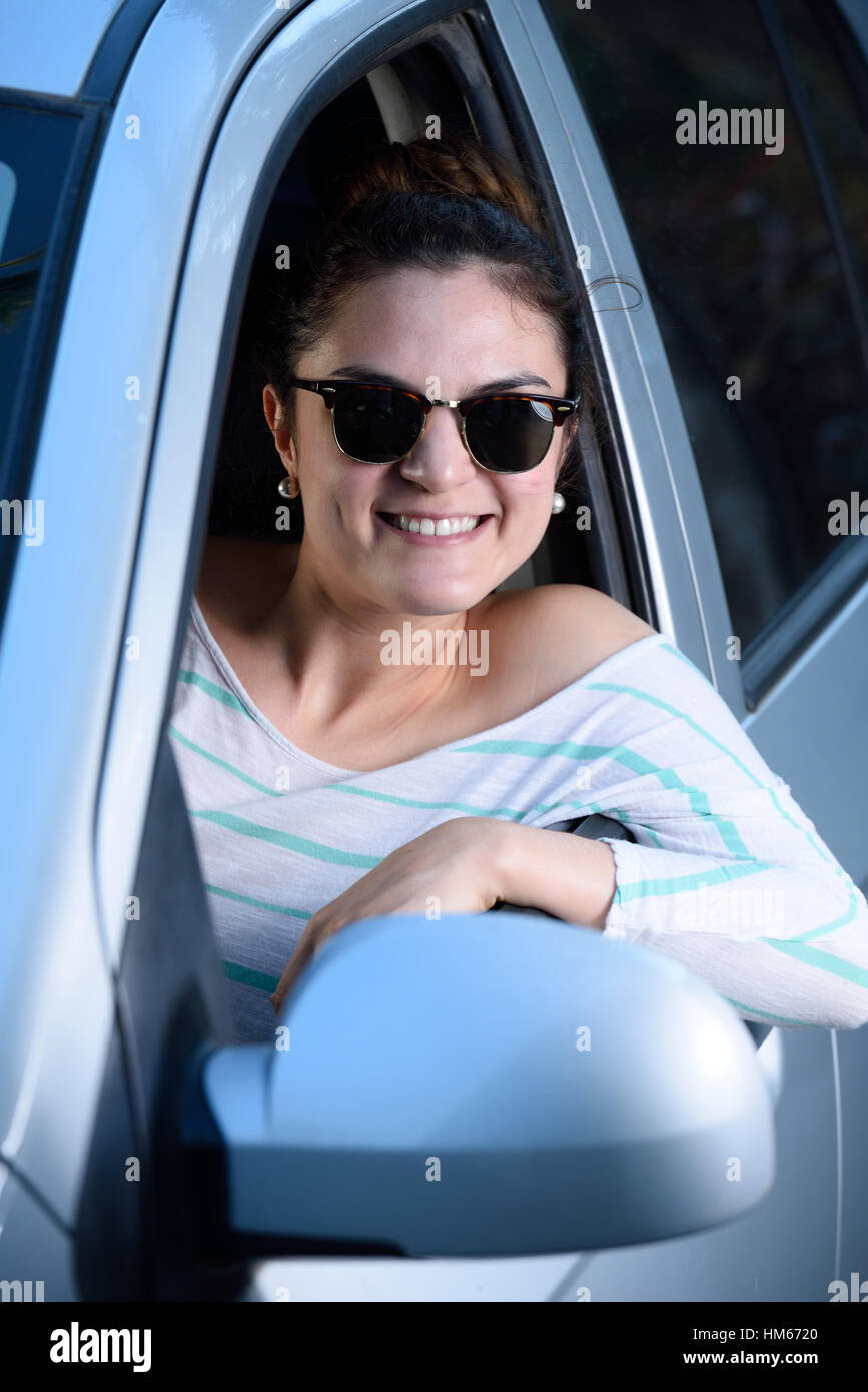 girl driving with the arm out of the window and smiling with sunglasses ...