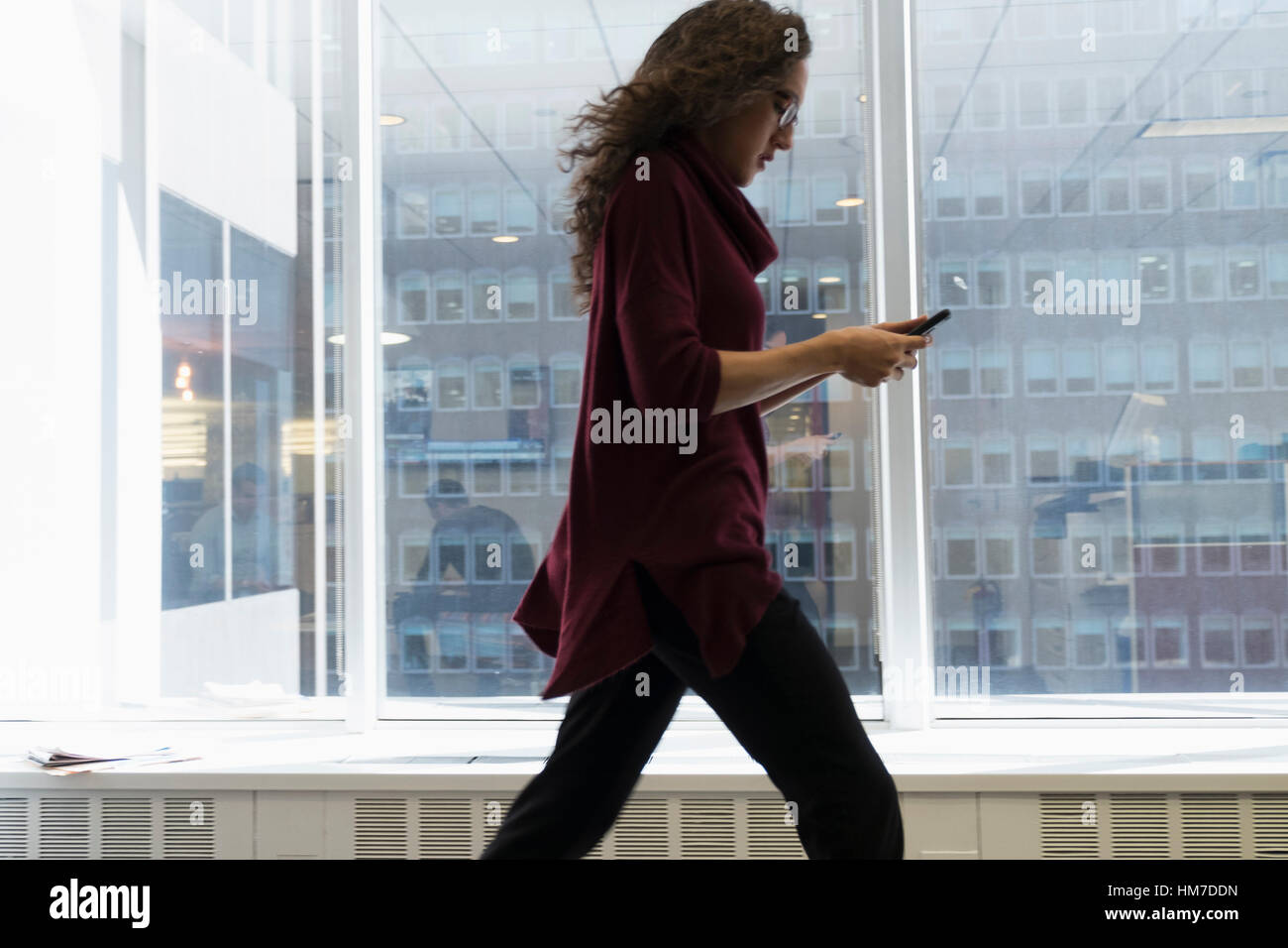 Young woman walking with mobile phone in front of window Stock Photo ...